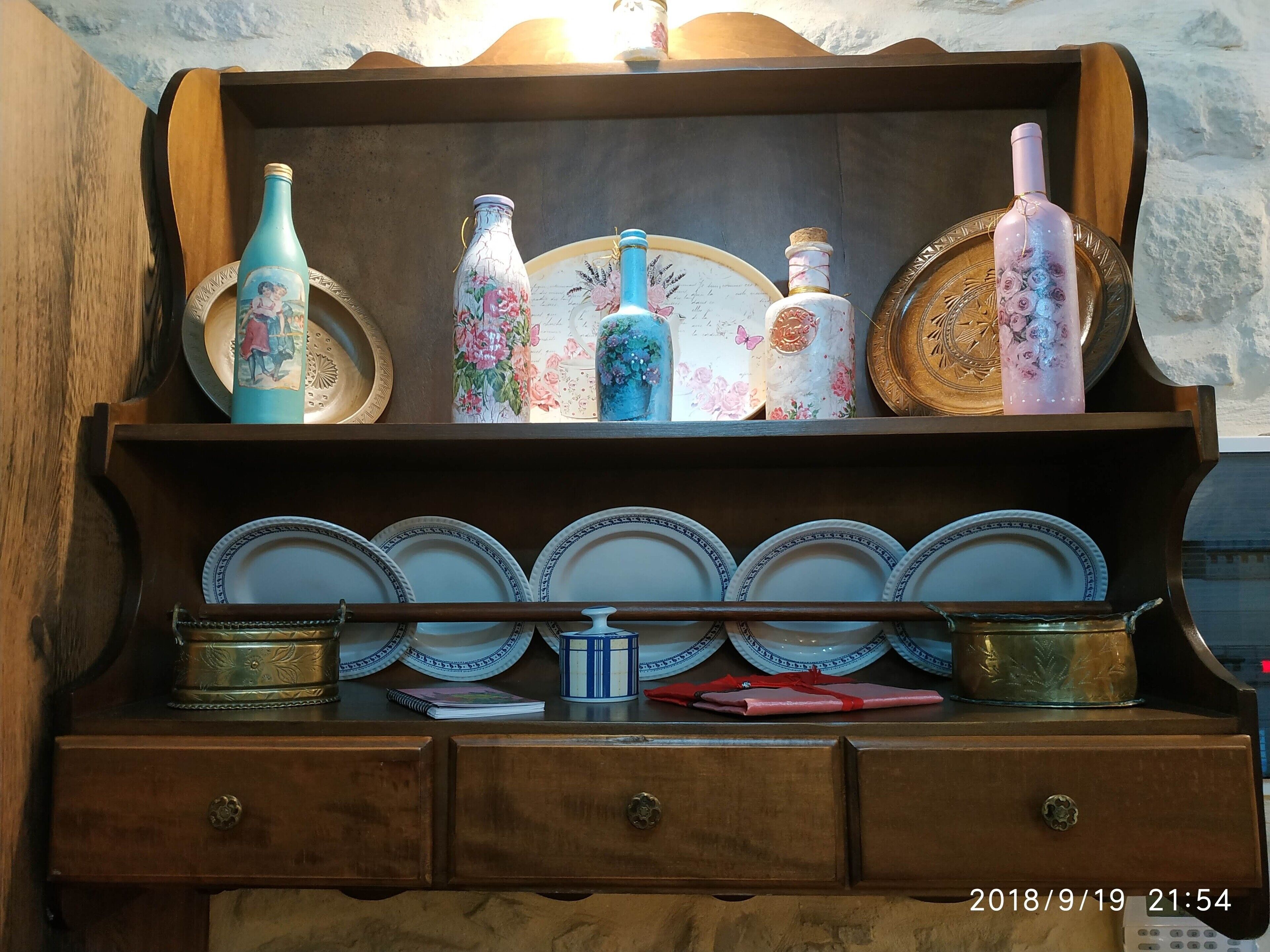 Um expositor de madeira com pratos decorativos, vasos e um livro pequeno.