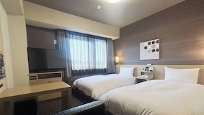 Quarto de hotel com duas camas, uma escrivaninha, televisão e janela com cortinas.