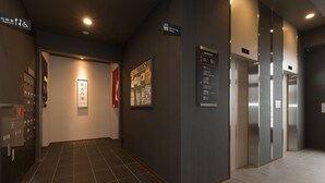 Área de elevadores moderna com painéis digitais, placa de banheiro e um cartaz na parede.