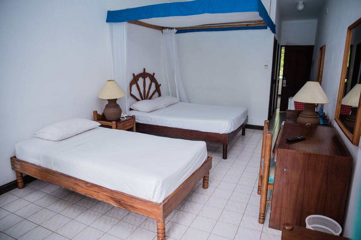 Quarto com duas camas de madeira, uma cômoda de madeira e um espelho.
