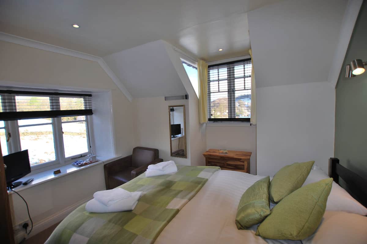 Quarto com cama, cadeira, escrivaninha, televisão e janela.