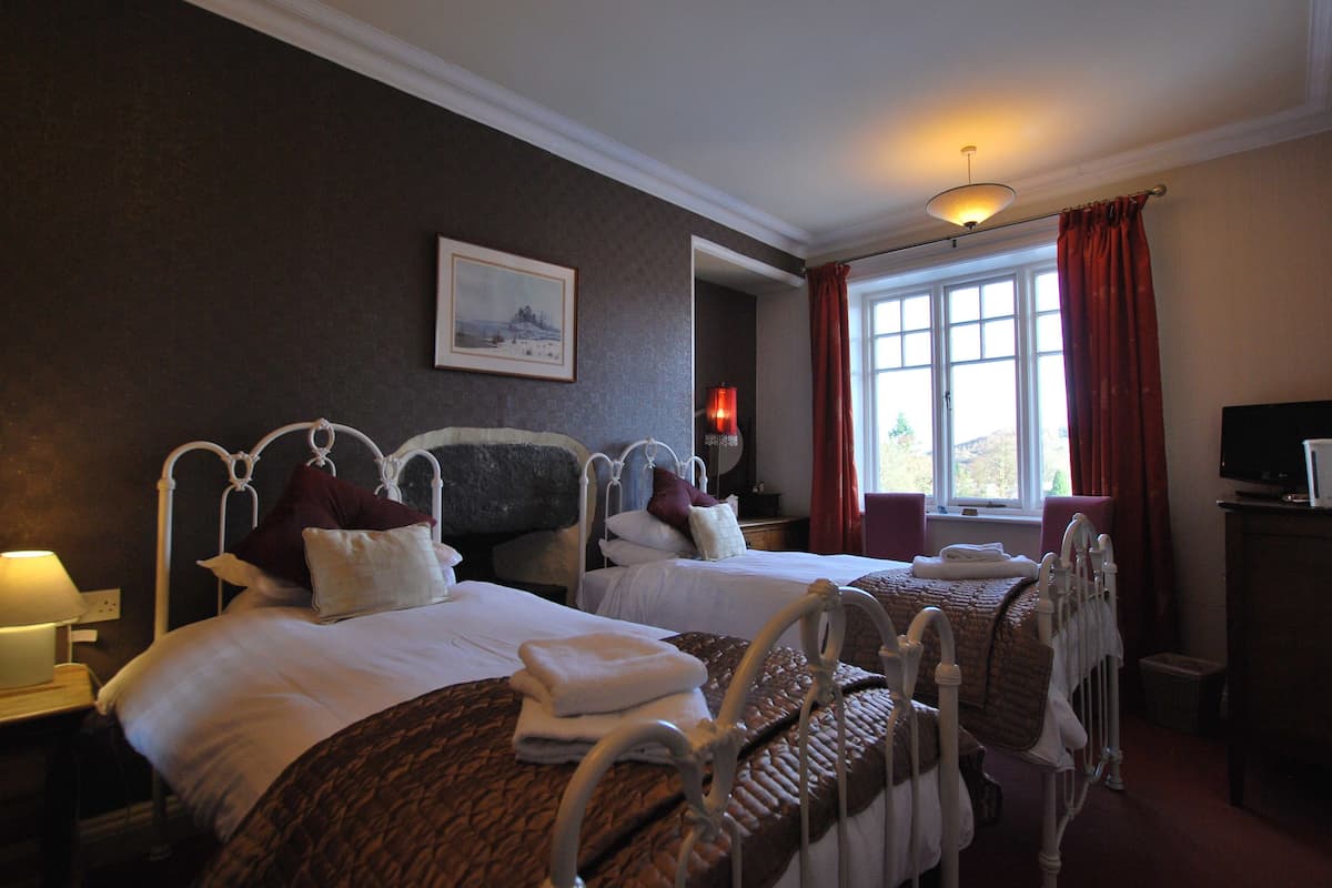 Quarto de hotel com duas camas, televisão e janela com cortinas.