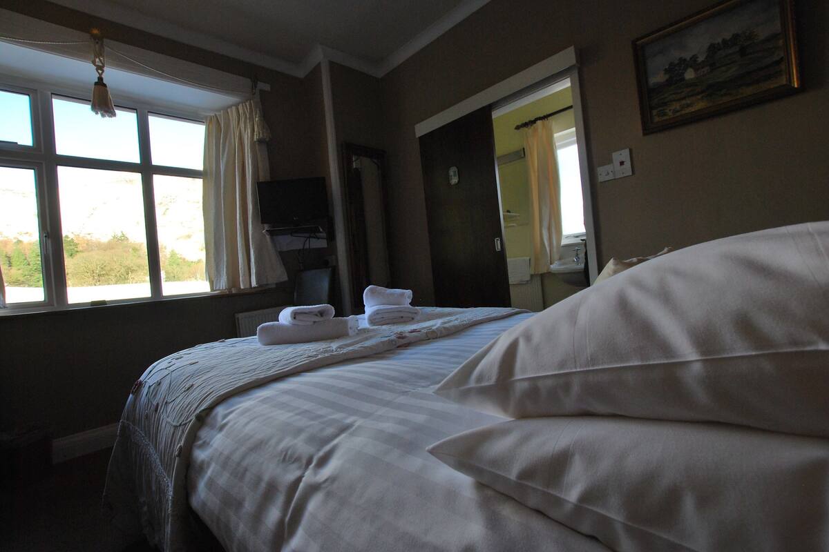 Quarto de hotel com uma cama grande, janela com cortinas, televisão de tela plana e um quadro na parede.