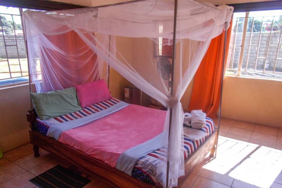 Uma cama com dossel, travesseiros e mesa de cabeceira com um ventilador.
