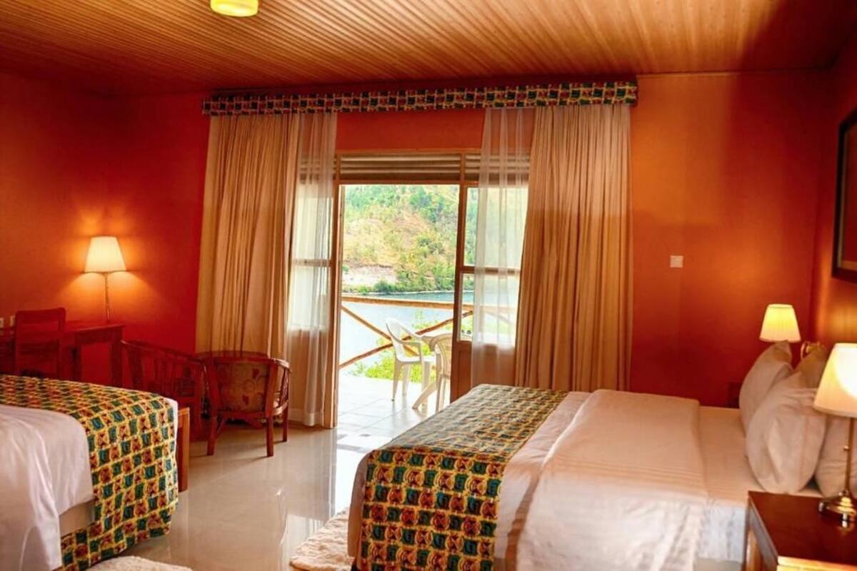 Quarto de hotel com duas camas, varanda e vista para um lago.