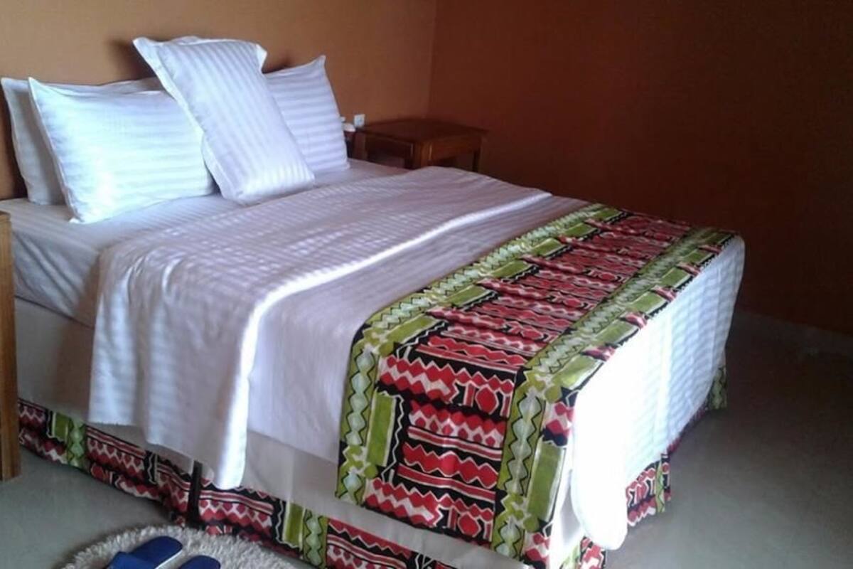 Cama bem arrumada com lençóis brancos e edredom estampado em cores vibrantes.