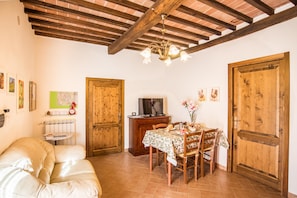 Um quarto acolhedor com teto de madeira, uma mesa de jantar com cadeiras, um sofá e uma TV em um móvel.