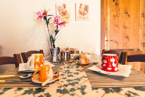 Uma mesa de jantar posta com diversos pratos, uma cafeteira e um vaso com flores.