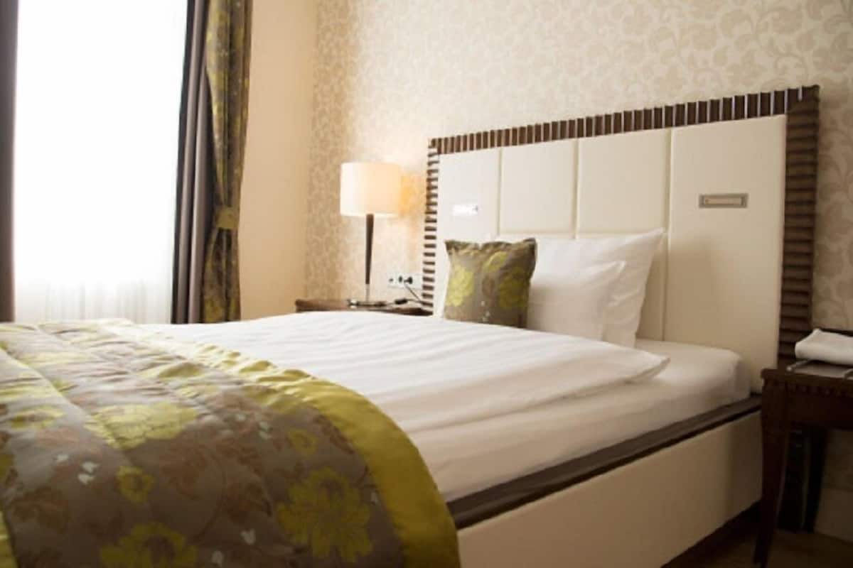 Quarto de hotel com uma cama grande, uma mesa de cabeceira com abajur e uma parede estampada.