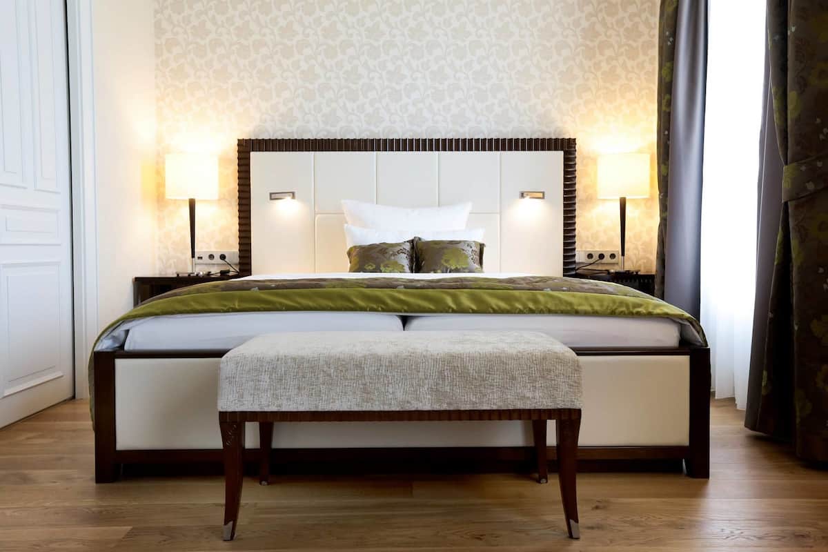 Quarto bem arrumado com uma cama grande, duas luminárias de cabeceira e um banquinho em frente à cama.