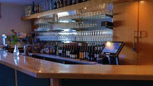 Uma área de bar com adega, lista de vinhos digital e variedade de garrafas.