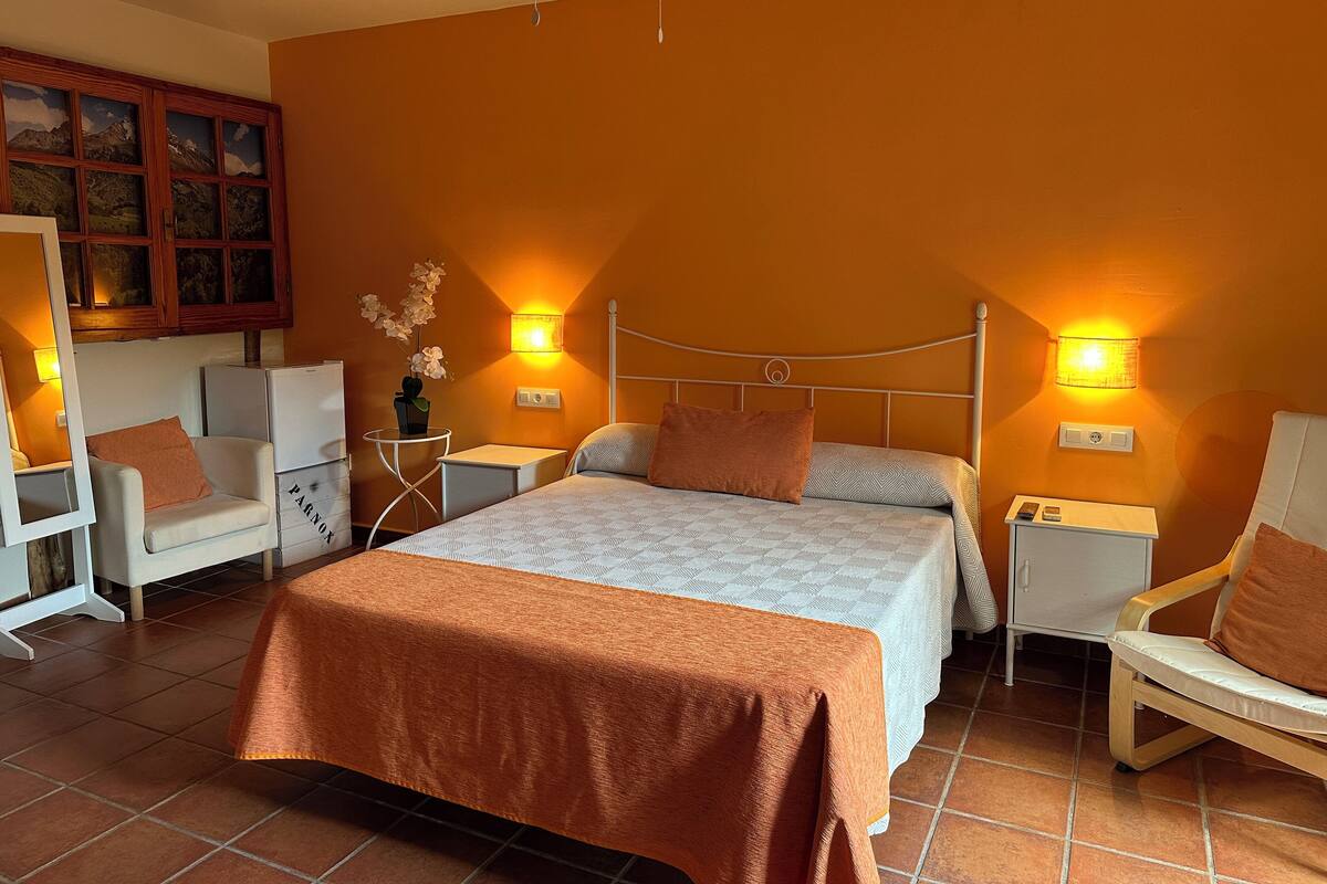 Quarto com cama, duas mesas de cabeceira, uma cadeira, uma mesinha e um ventilador de teto.