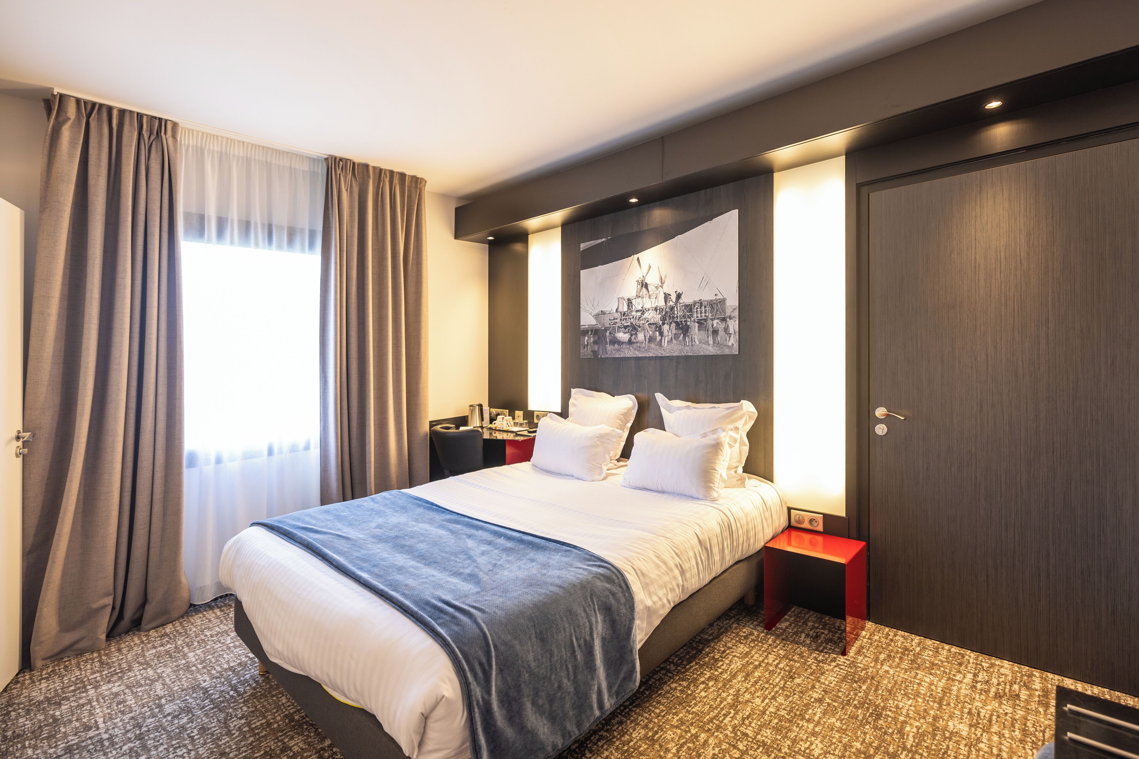 Quarto de hotel com uma cama grande, mesa de cabeceira, escrivaninha e guarda-roupa.