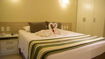 Quarto de hotel com cama bem arrumada, mesa de cabeceira com abajur e guarda-roupa.