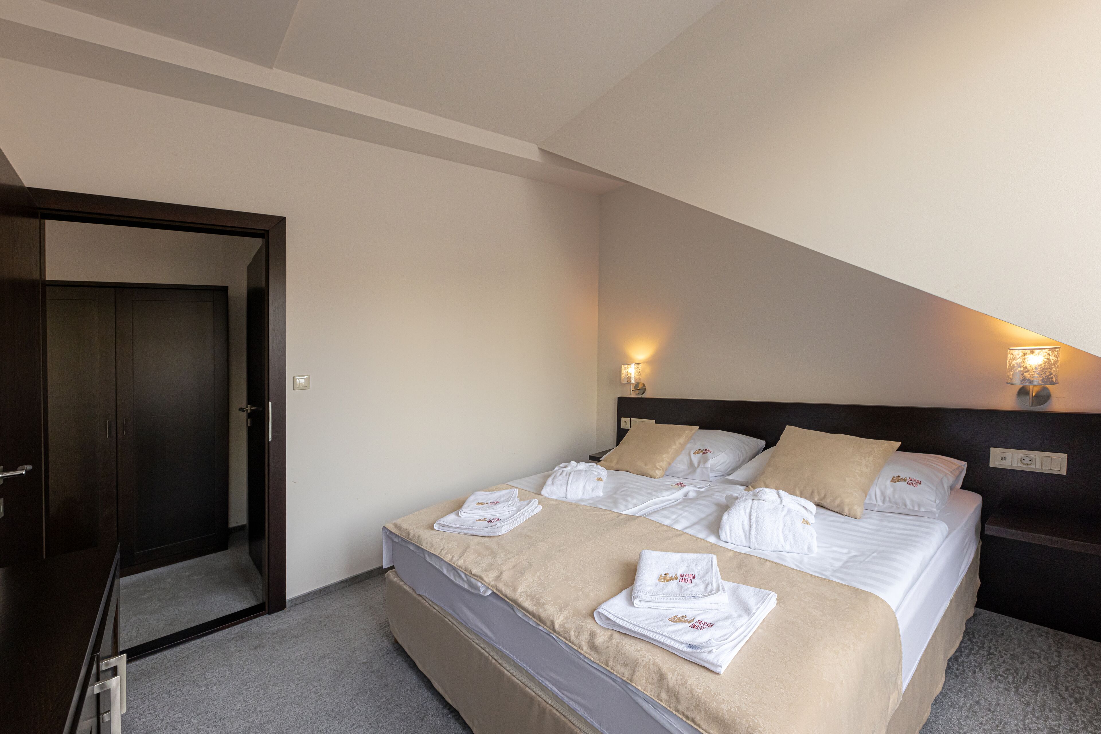 Quarto de hotel com cama, guarda-roupa e mesa de cabeceira com abajur.