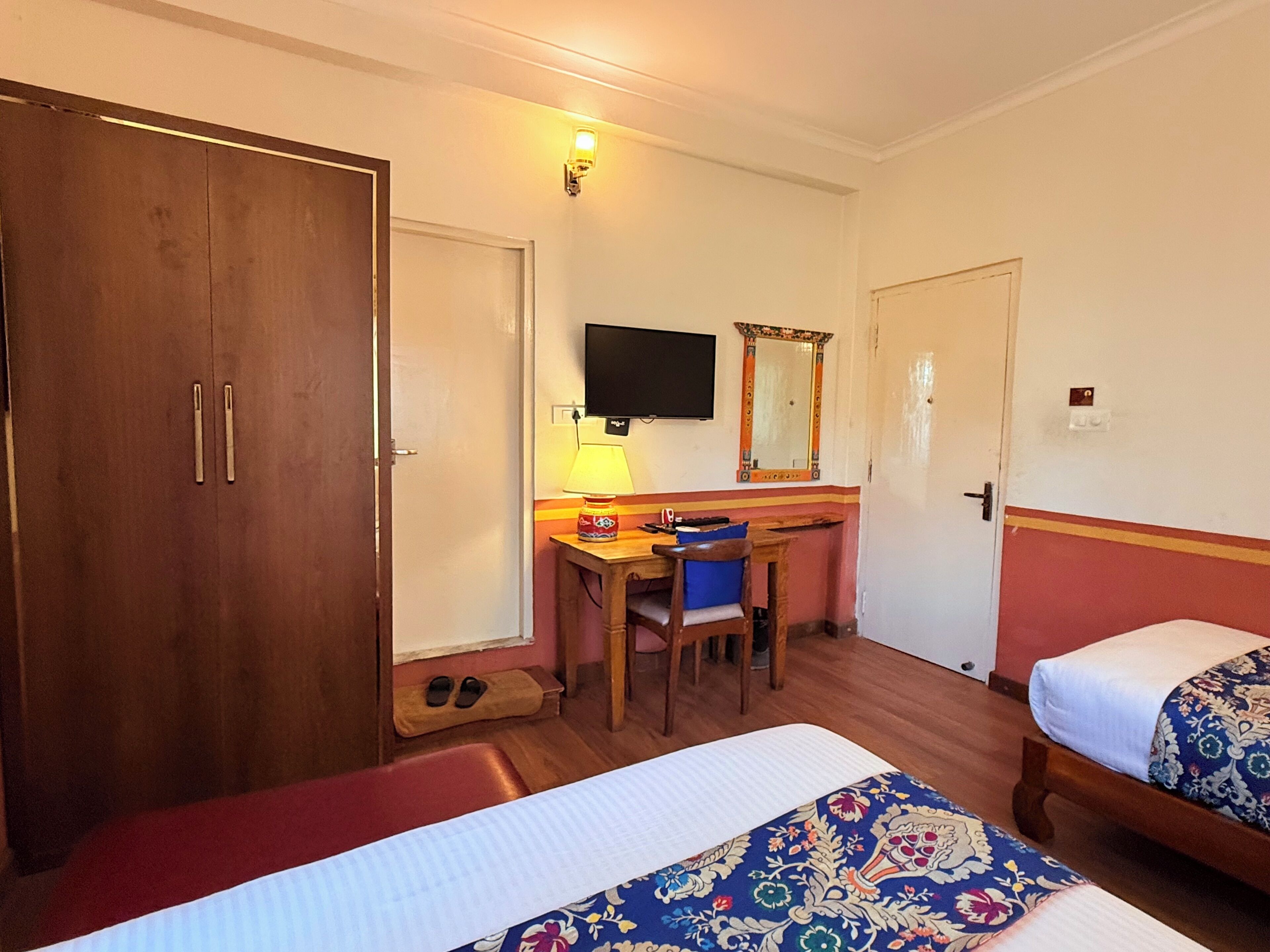 Quarto de hotel com duas camas, uma mesa de trabalho com cadeira, televisão e um espelho.