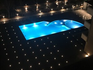 Piscina no terraço iluminada em azul, com luzes uniformemente distribuídas ao redor.