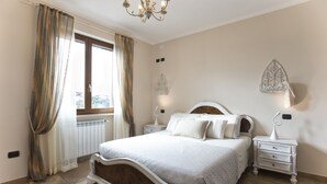 Quarto com uma cama grande, duas mesas de cabeceira, uma janela com cortinas e um candelabro.
