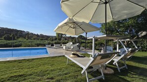 Área de piscina com espreguiçadeiras, guarda-sóis e vista para uma encosta.
