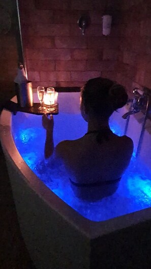 Uma pessoa em uma banheira com iluminação azul, segurando uma bandeja com copos.