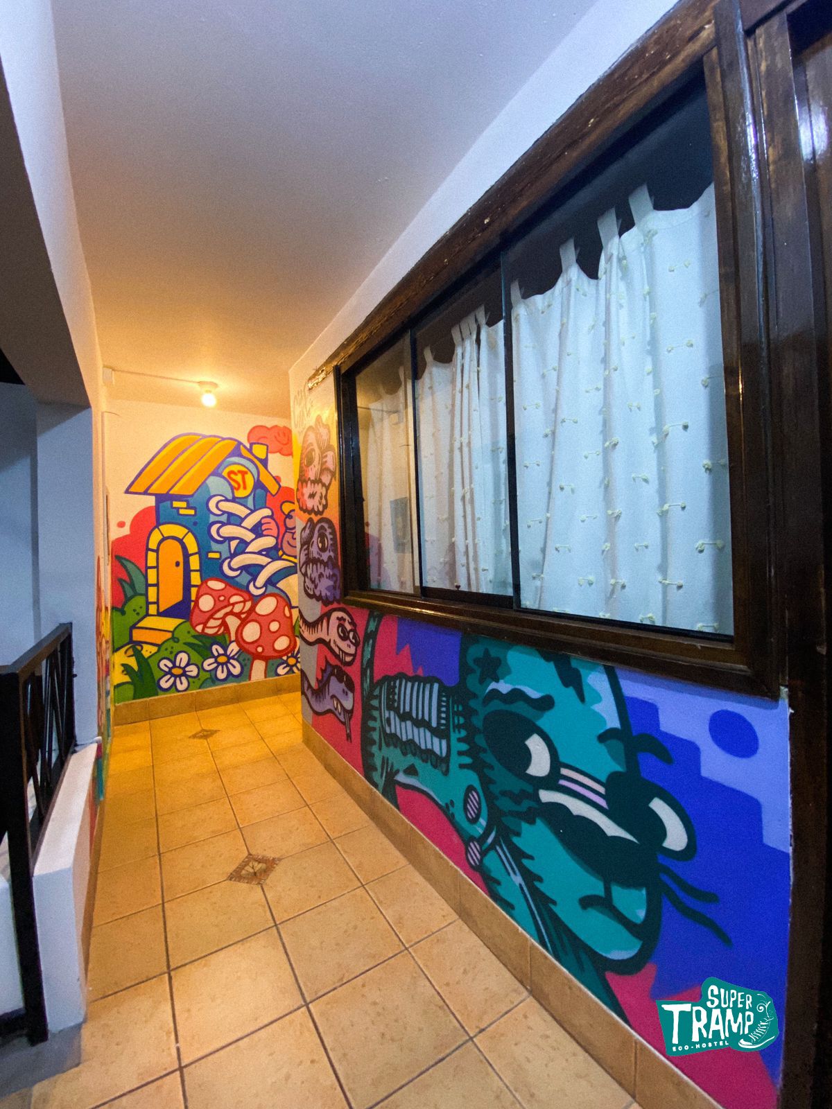 Um corredor com arte de grafite colorida nas paredes, uma janela com cortinas brancas e chão de azulejos.