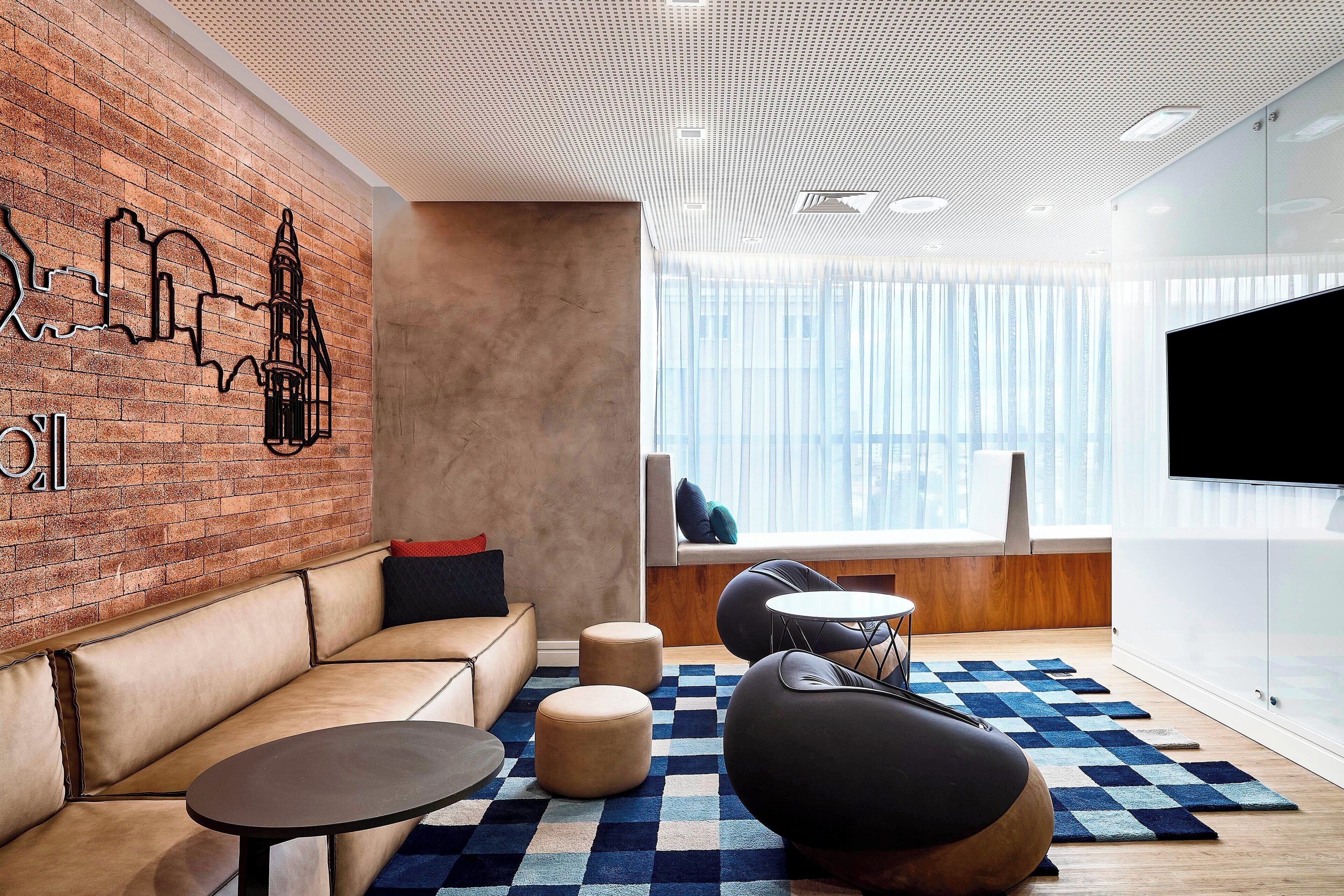 Um lounge moderno com parede de tijolos, sofá de couro, mesas redondas e tapete xadrez.