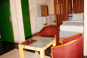 Quarto de hotel com cama, escrivaninha com cadeira, armário pequeno e porta verde.