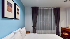Quarto de hotel com cama, escrivaninha, cadeira e duas fotos emolduradas na parede.