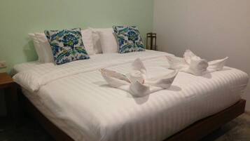 Uma cama bem arrumada com lençóis brancos e almofadas estampadas com motivos florais, uma mesinha de cabeceira de madeira e uma pequena mesa com abajur.