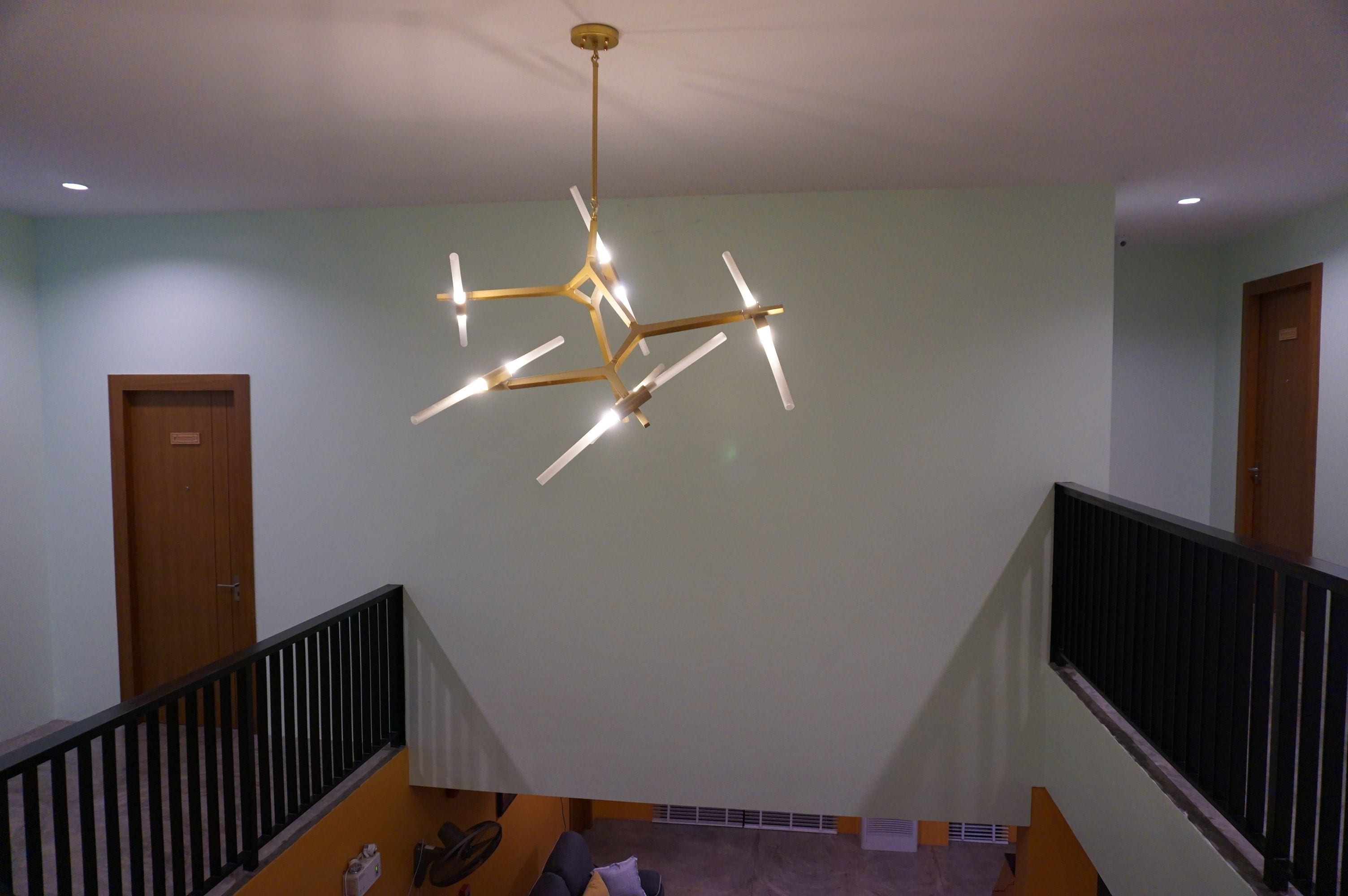 Um interior com vários níveis, com um lustre moderno, portas de madeira e guarda-corrimão preto.