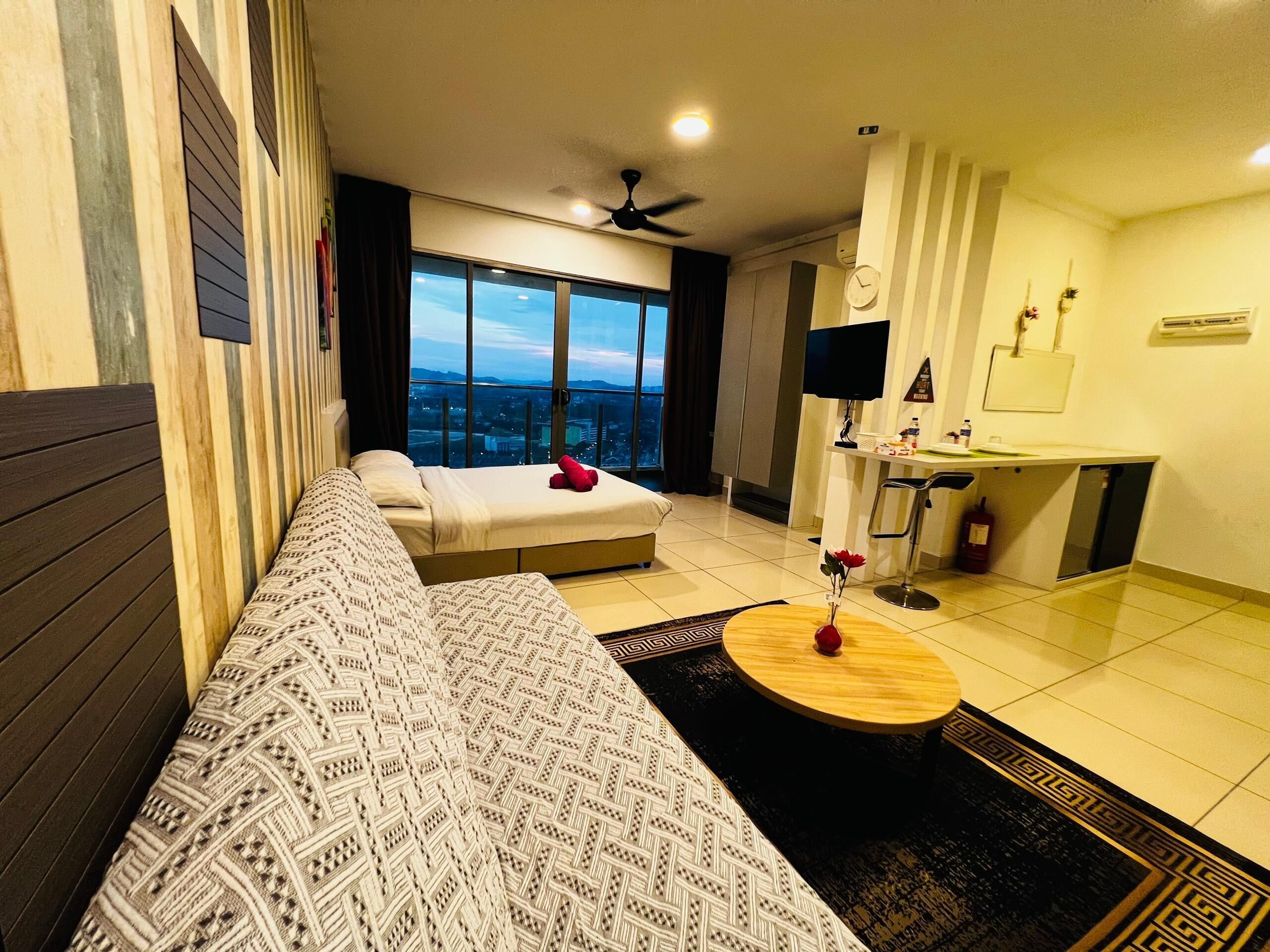 Quarto de hotel com cama, sofá, televisão, escrivaninha e vista para a cidade.