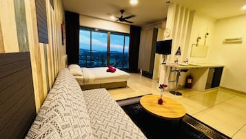 Quarto de hotel com cama, sofá, televisão, escrivaninha e vista para a cidade.