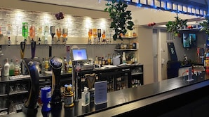 Uma área de bar com vários dispensadores de bebidas, um monitor de computador e uma variedade de garrafas.