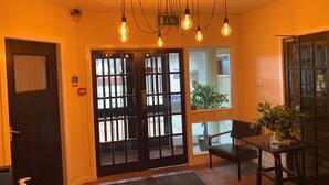 Um saguão de hotel com uma porta de madeira escura, um balcão de recepção e uma área de estar com uma planta.