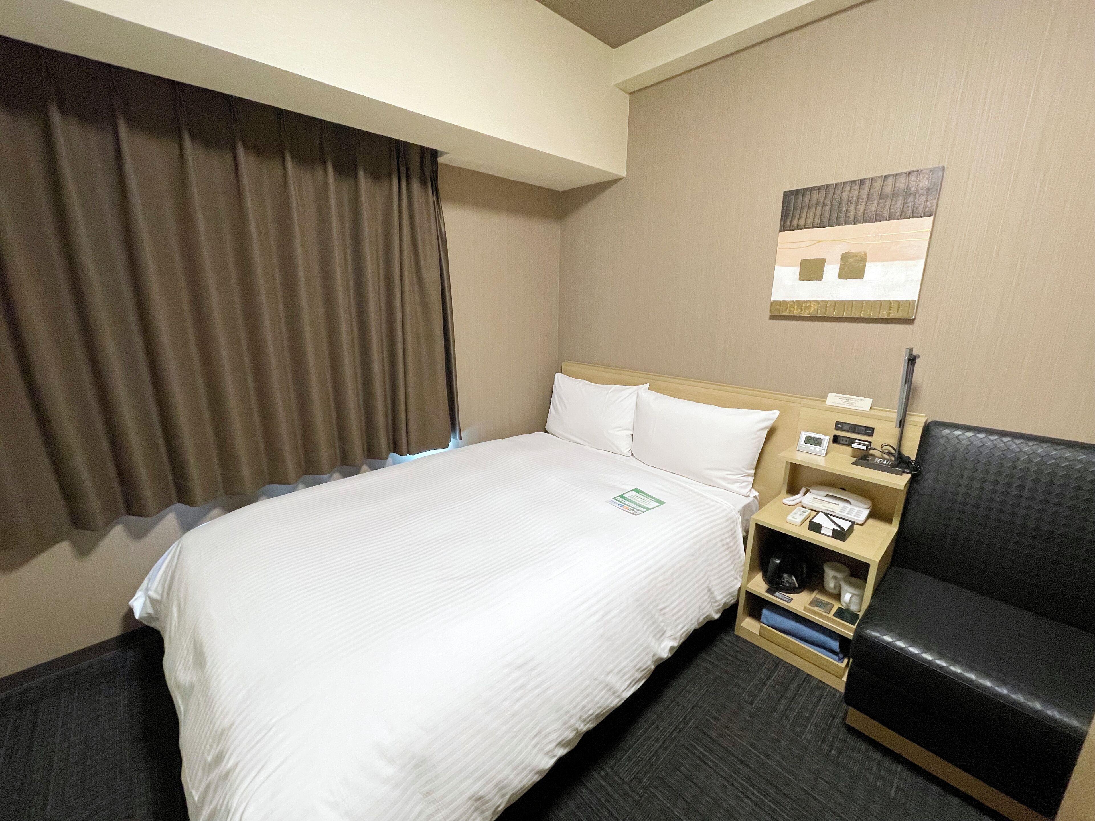 Quarto de hotel com uma cama, uma escrivaninha com telefone e uma poltrona de couro preto.