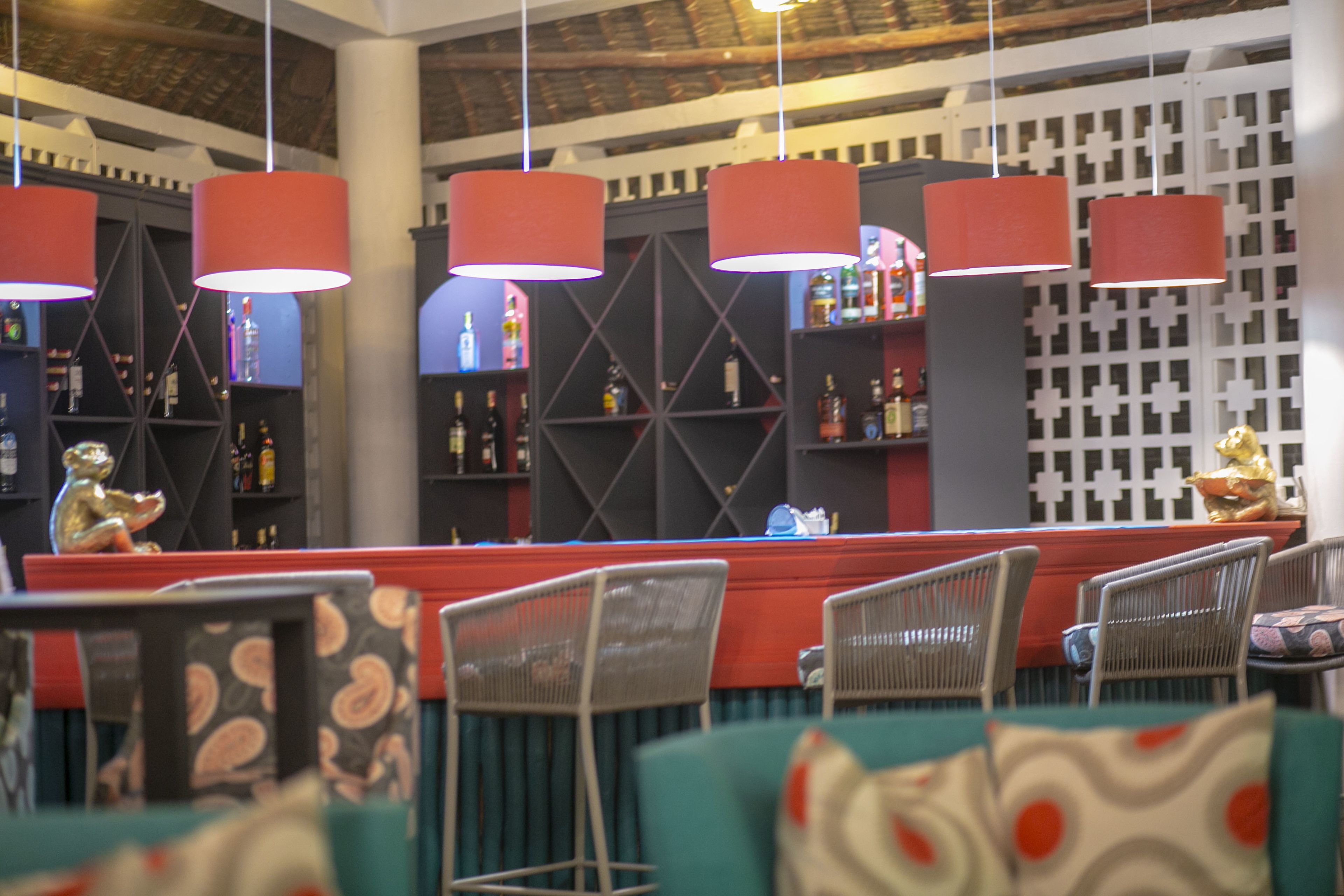 Uma área de bar com luminárias pendentes vermelhas, cadeiras de vime e um painel de parede estampado.