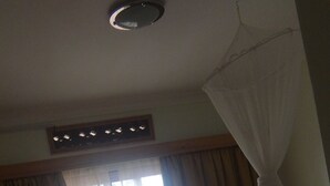 Quarto com cama, janela com cortinas, mosquiteiro e tapete estampado com flores.
