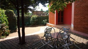 Uma área de pátio com mesa e cadeiras, cercada por vegetação e um muro de tijolos.