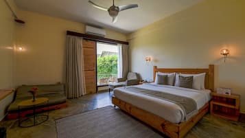Quarto com uma cama grande, ventilador de teto, janela com cortinas, uma mesinha com um vaso e criado-mudo com abajur.