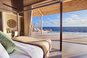 Quarto com cama grande, vista para o oceano e deck de madeira com espreguiçadeiras.