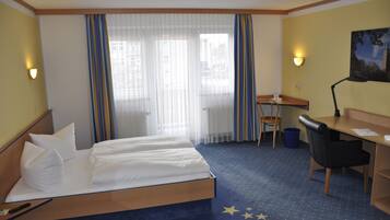 Quarto de hotel com cama, escrivaninha, cadeira e abajur.