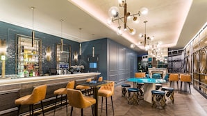 Uma área de bar com balcão extenso, banquetas e uma mesa central com cadeiras.