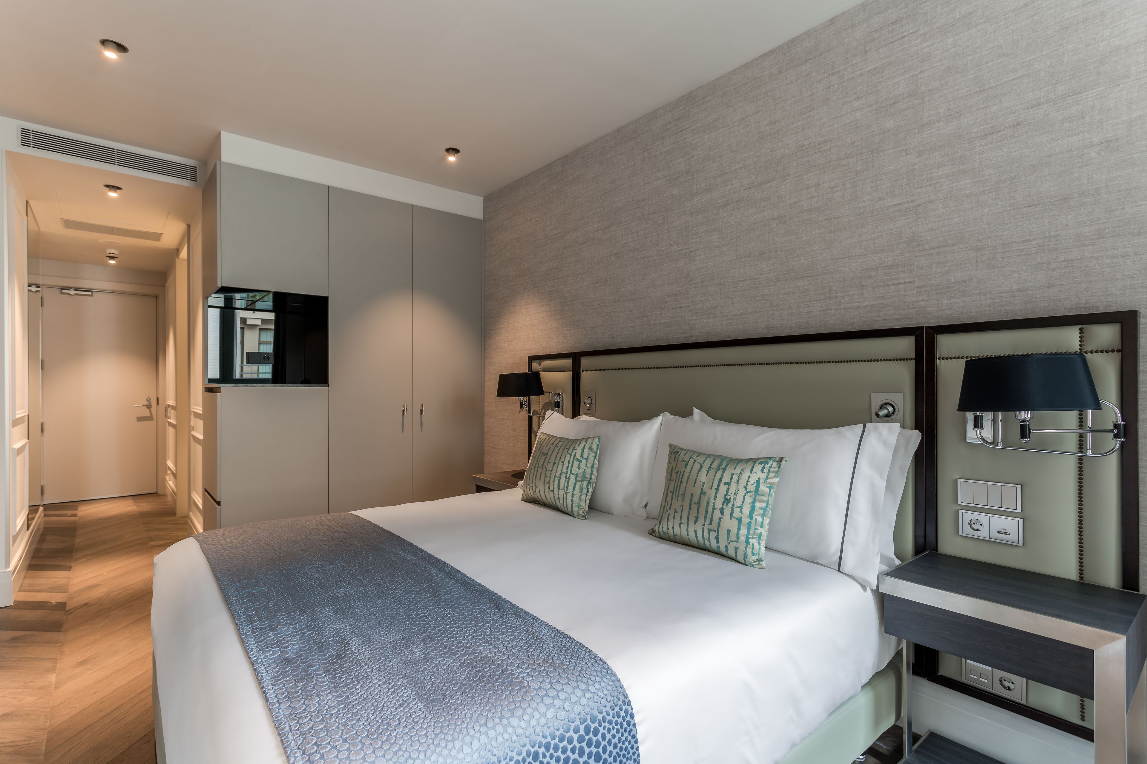 Quarto de hotel moderno com uma cama grande, mesa de cabeceira, televisão e guarda-roupa.