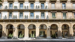 Um edifício de vários andares com arquitetura clássica, com janelas em arco e varandas com plantas.