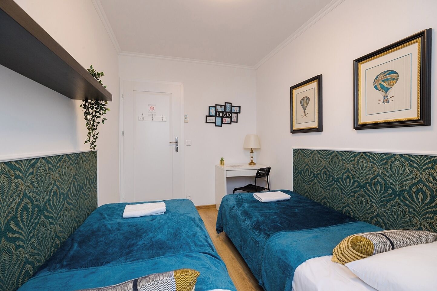 Quarto de hotel com duas camas, uma escrivaninha, uma cadeira, uma luminária e quadros nas paredes.