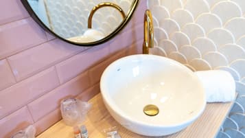 Casa de banho com uma pia branca, uma torneira dourada e um espelho. Há produtos de higiene pessoal no balcão.