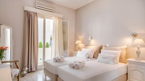 Quarto de hotel com duas camas, área de estar e varanda com cortinas.