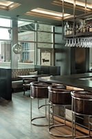 Uma área de bar com banquetas de couro, um balcão e uma vitrine de vidro com garrafas.