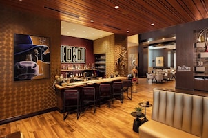 Uma área de bar com teto de madeira, balcão com banquetas e parede com um grande letreiro 'HOKU'.