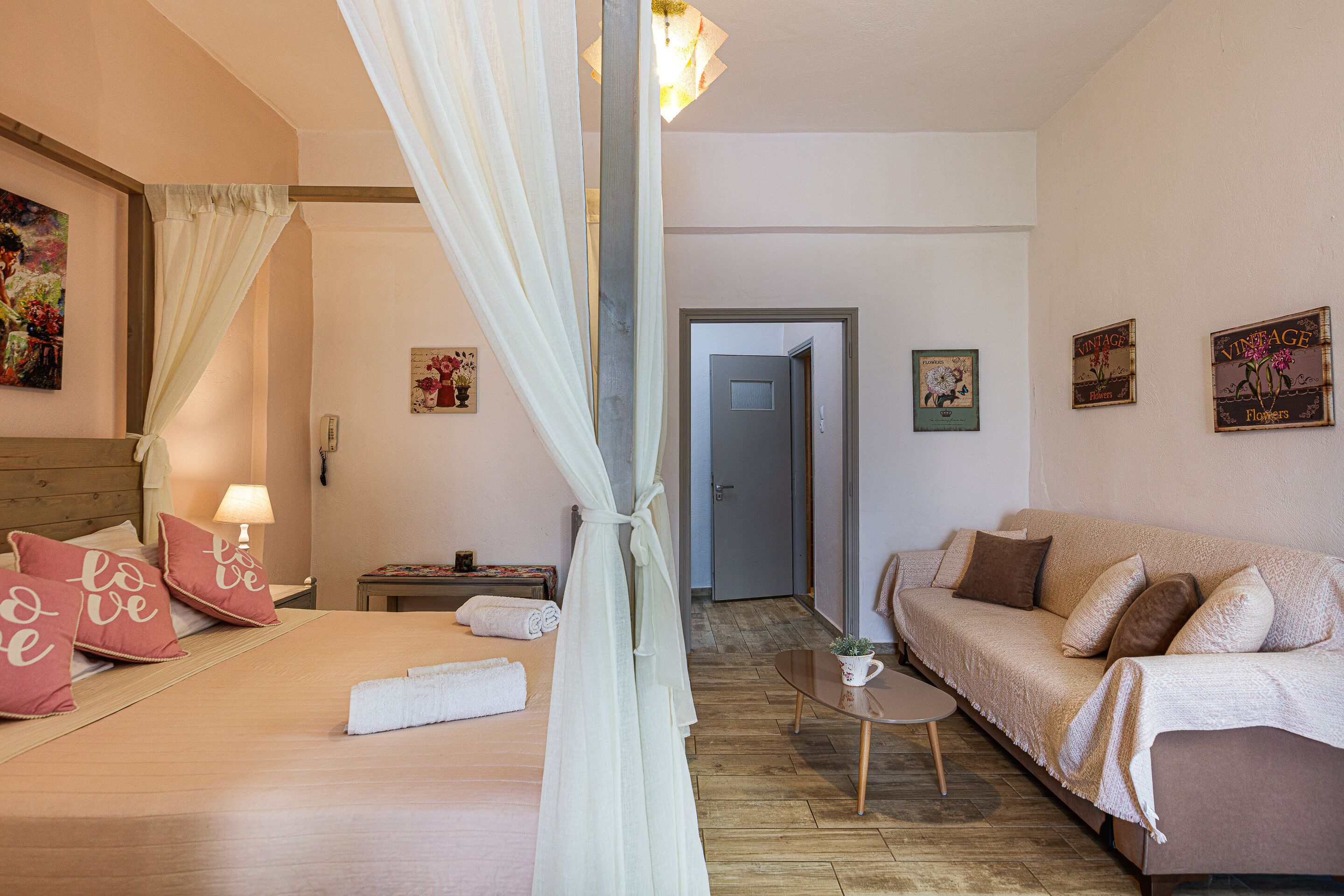 Quarto de hotel com cama, sofá, mesinha e porta que dá para outro quarto.